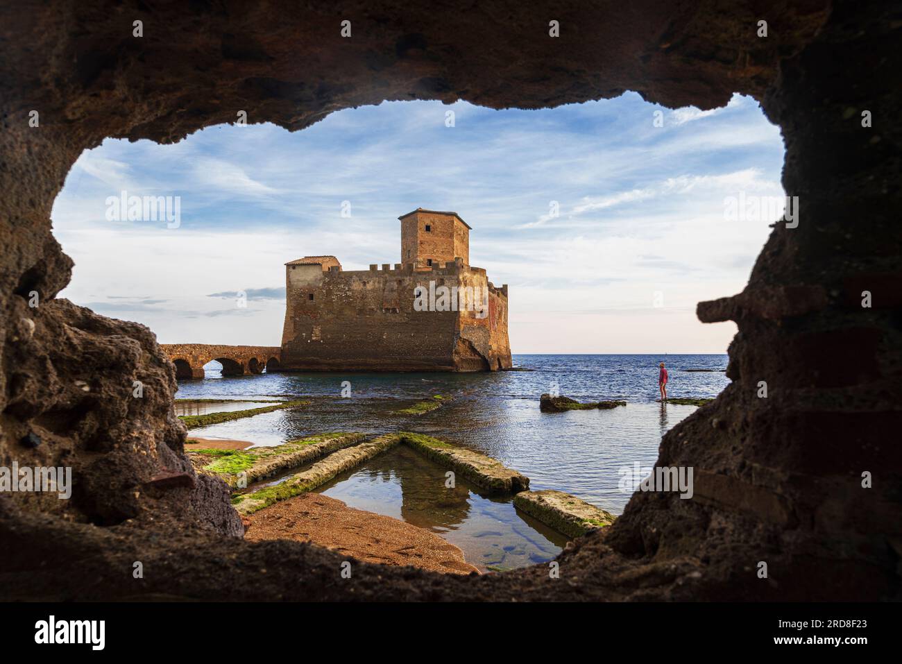 Tourist admiring the castle of Torre Astura seen through a cave in the ...