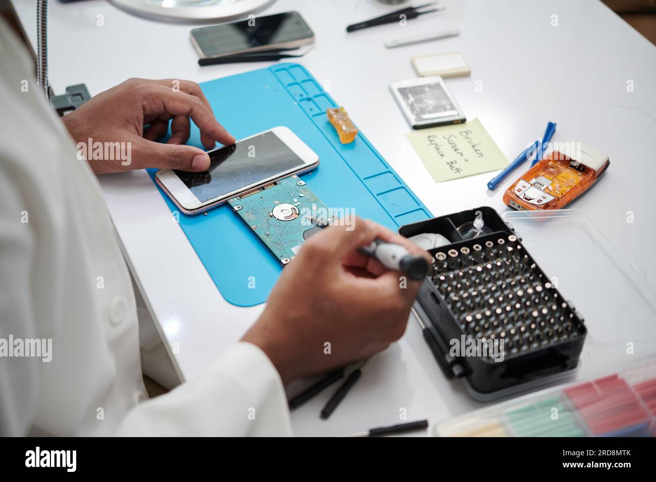 Closeup image of technician reassembling hard drive and smartphone ...