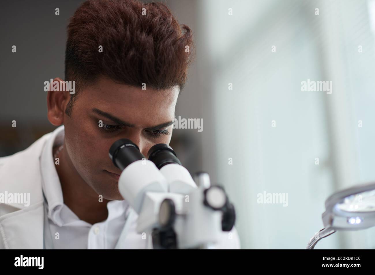 Serious Indian engineer looking into microscope Stock Photo - Alamy