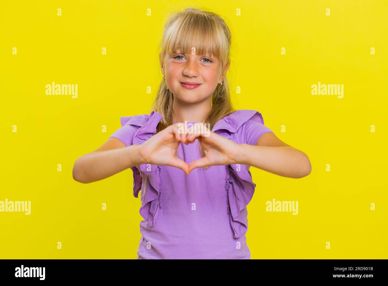 I love you. Smiling young cute blonde school girl makes heart gesture ...