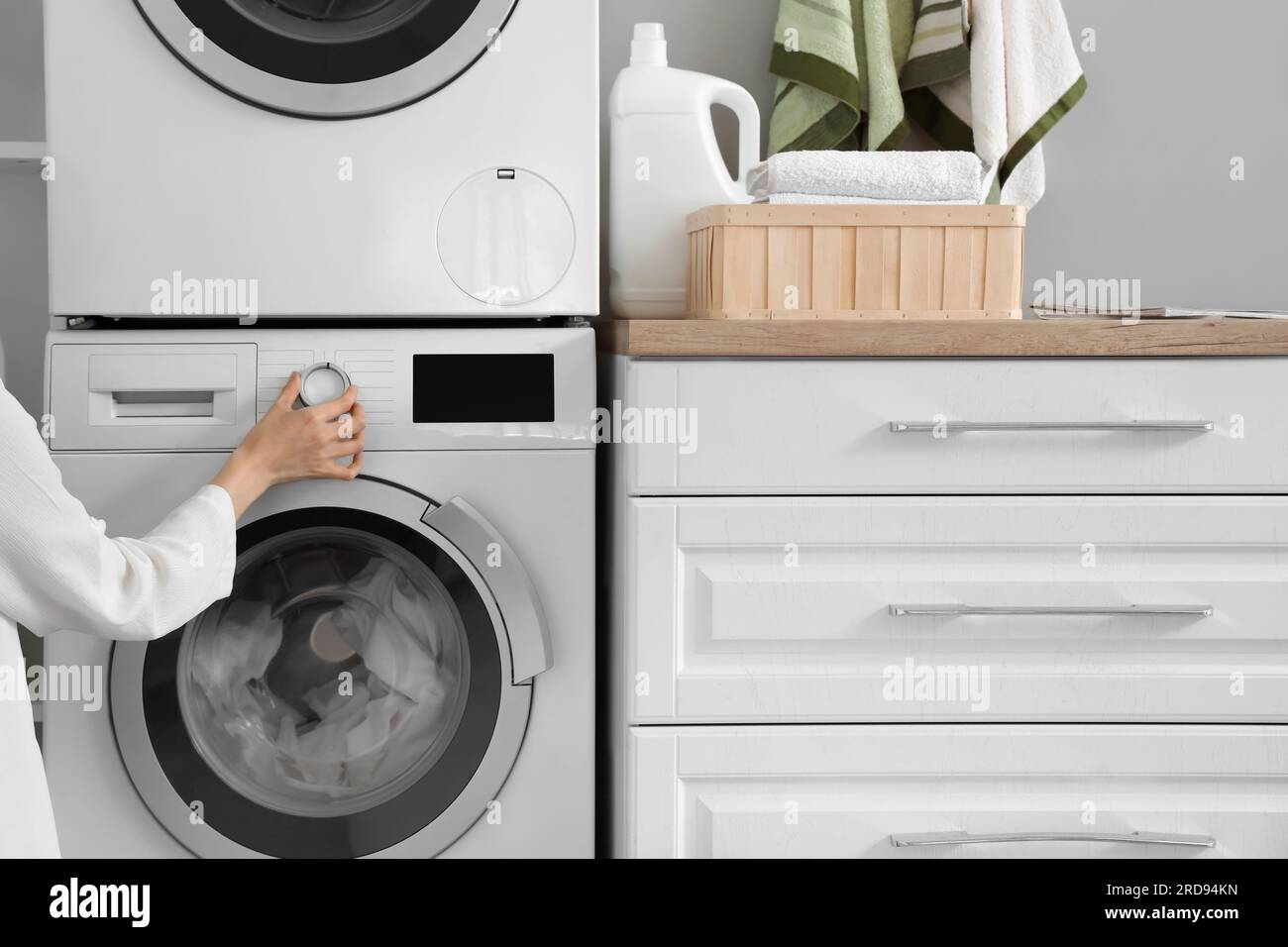 Woman setting up washing machine with dirty clothes in laundry room ...