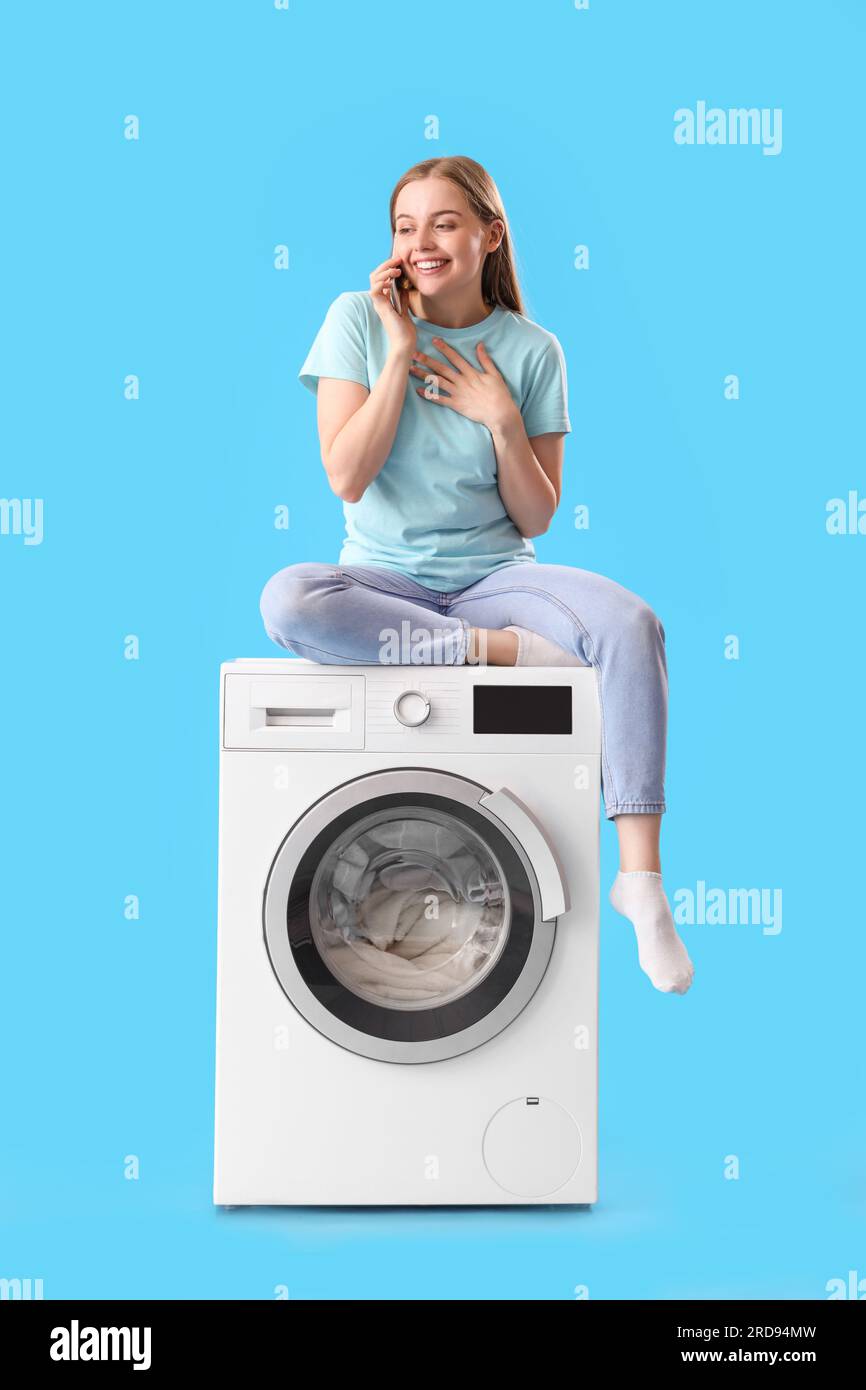 Pretty young woman sitting on washing machine and talking by mobile ...