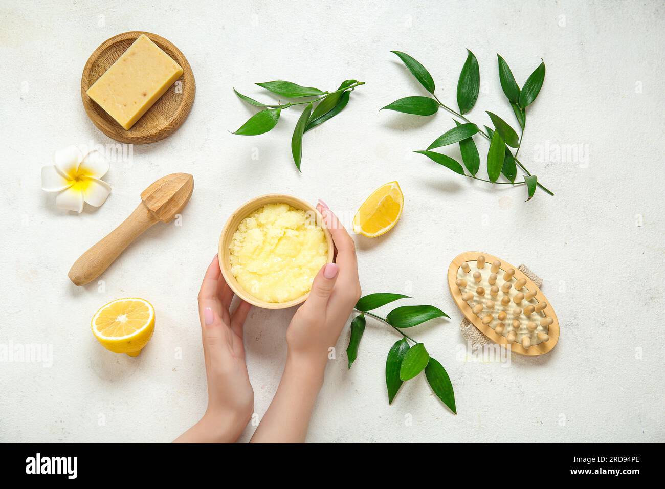 Bowl of lemon body scrub with juicer and bath supplies on white ...