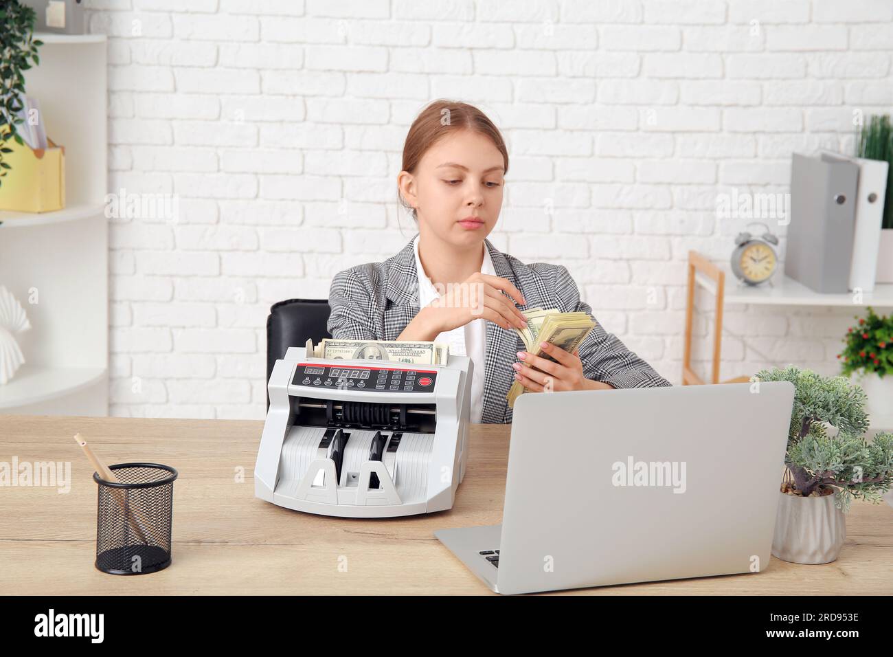 Young woman in business suit counting money at table with laptop and ...