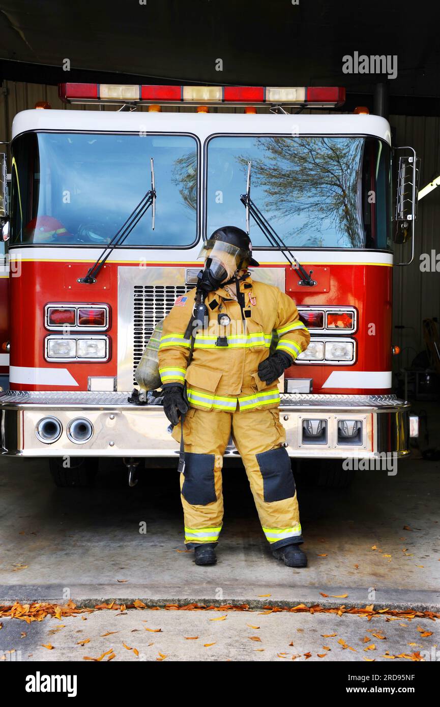 Woman firefighter stands in front of fire truck at fire station. She is ...