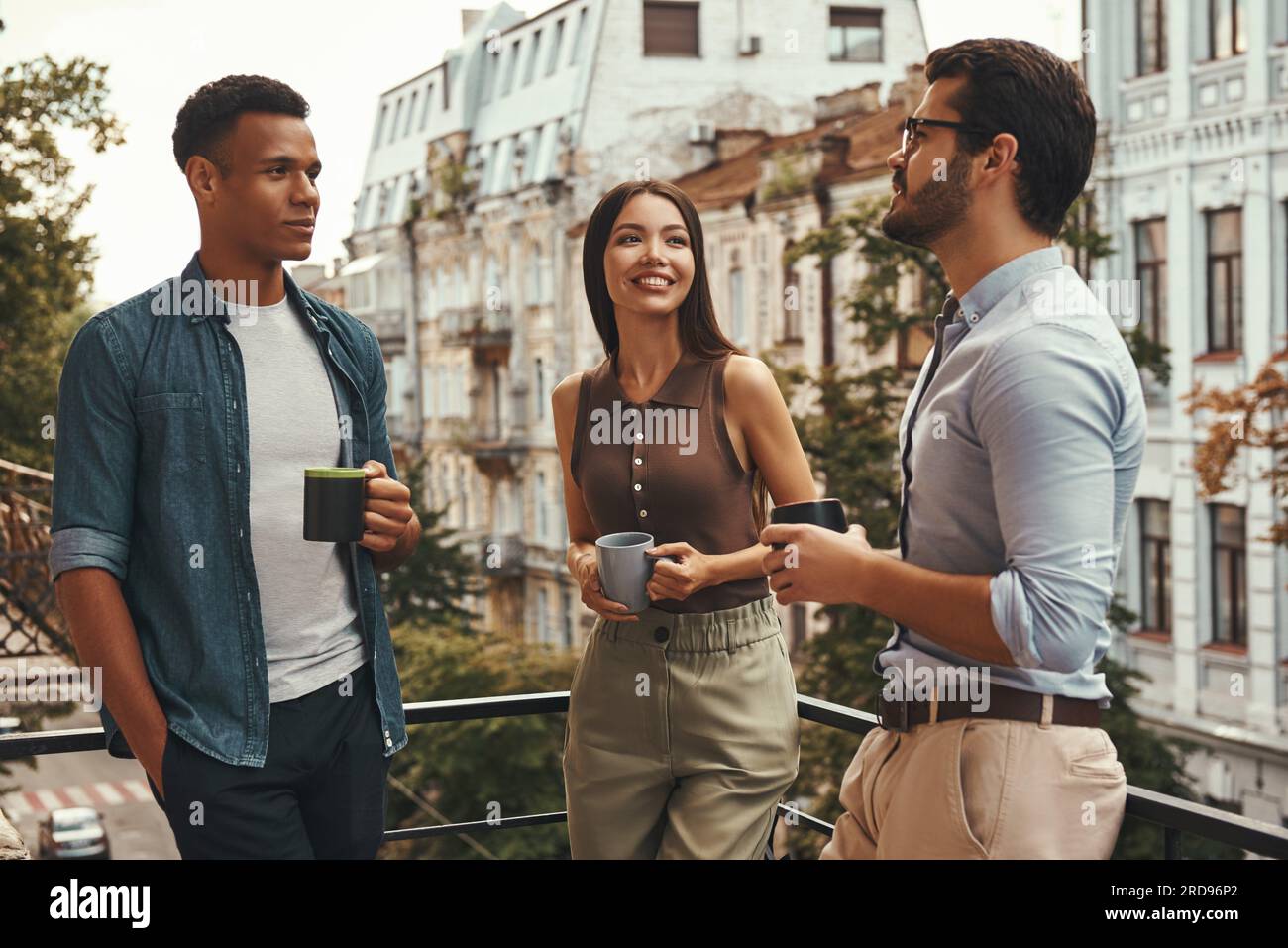 Coffee break. Young cheerful colleagues in casual wear holding cups and ...