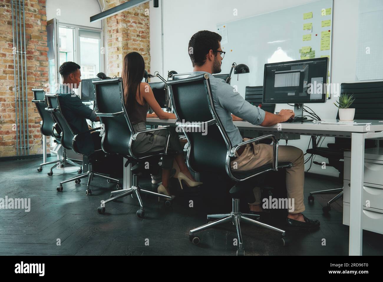 Office routine. Back view of young employees working on computers while ...