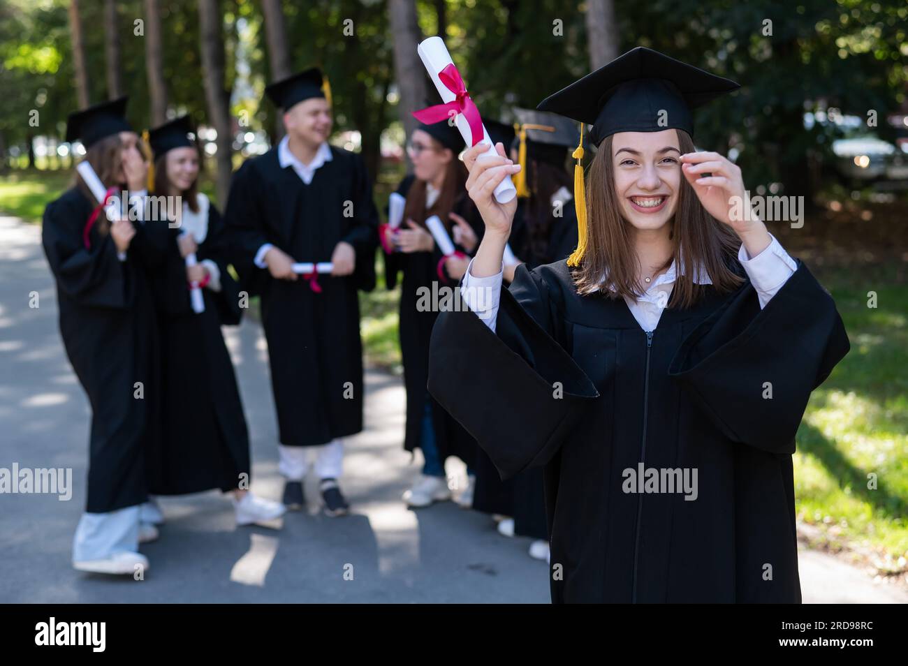 Group of happy students in graduation gowns outdoors. A young girl ...