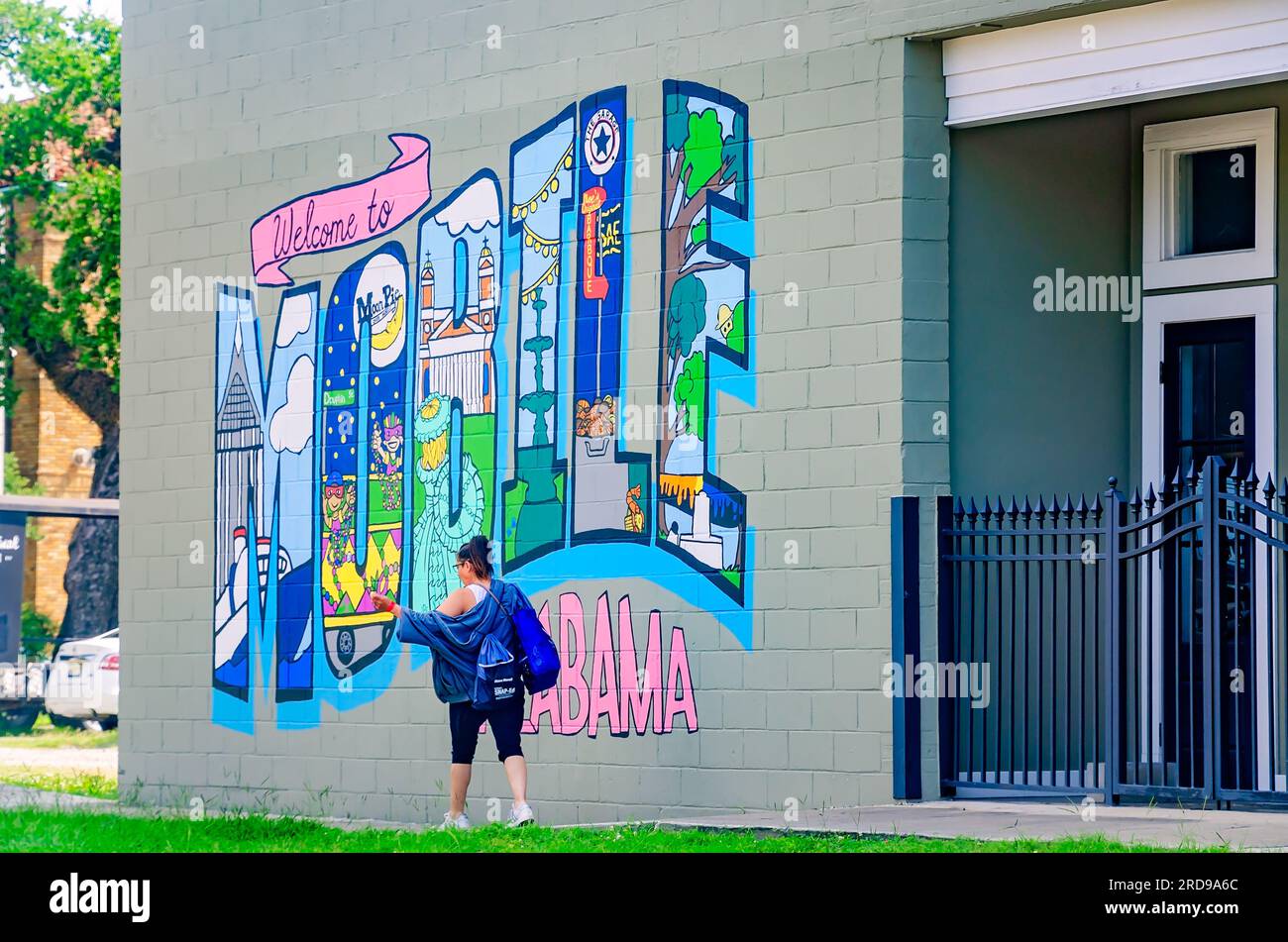 A woman walks past a postcard mural welcoming visitors to Mobile, June ...