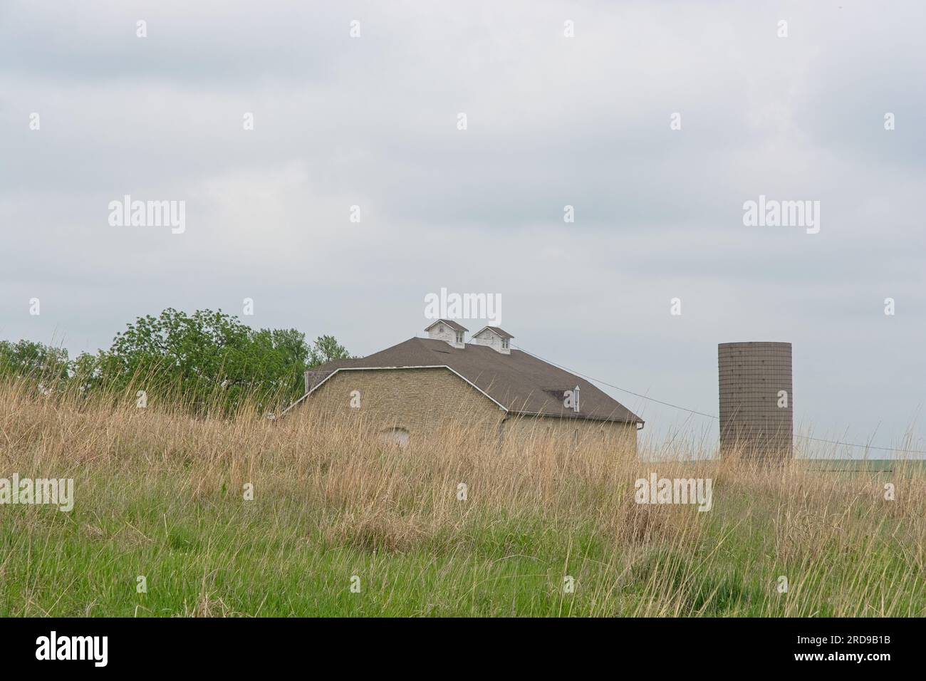 Limestone barn and silo behind hill rise lined with dried hay stalks on ...