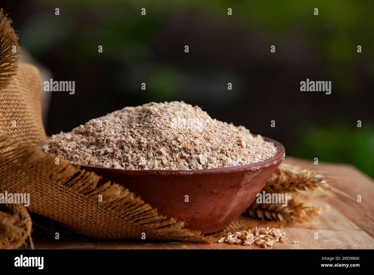 Wheat bran in a clay bowl and ears of wheat on a burlap background ...