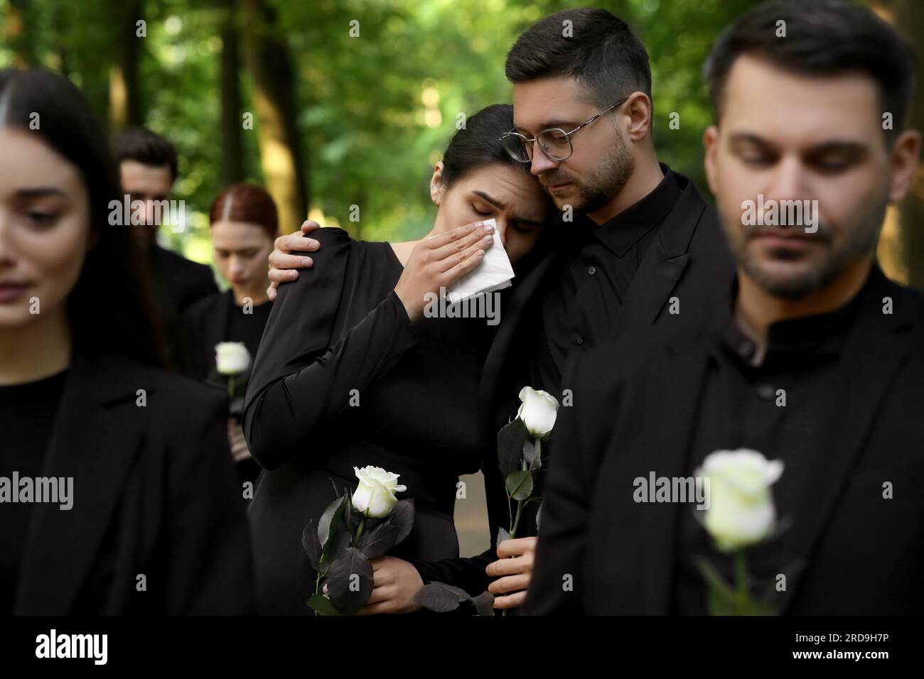 Funeral ceremony. Sad people with white rose flowers mourning outdoors ...
