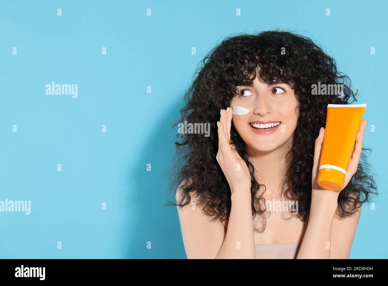 Beautiful young woman with tube of sunscreen applying sun protection ...