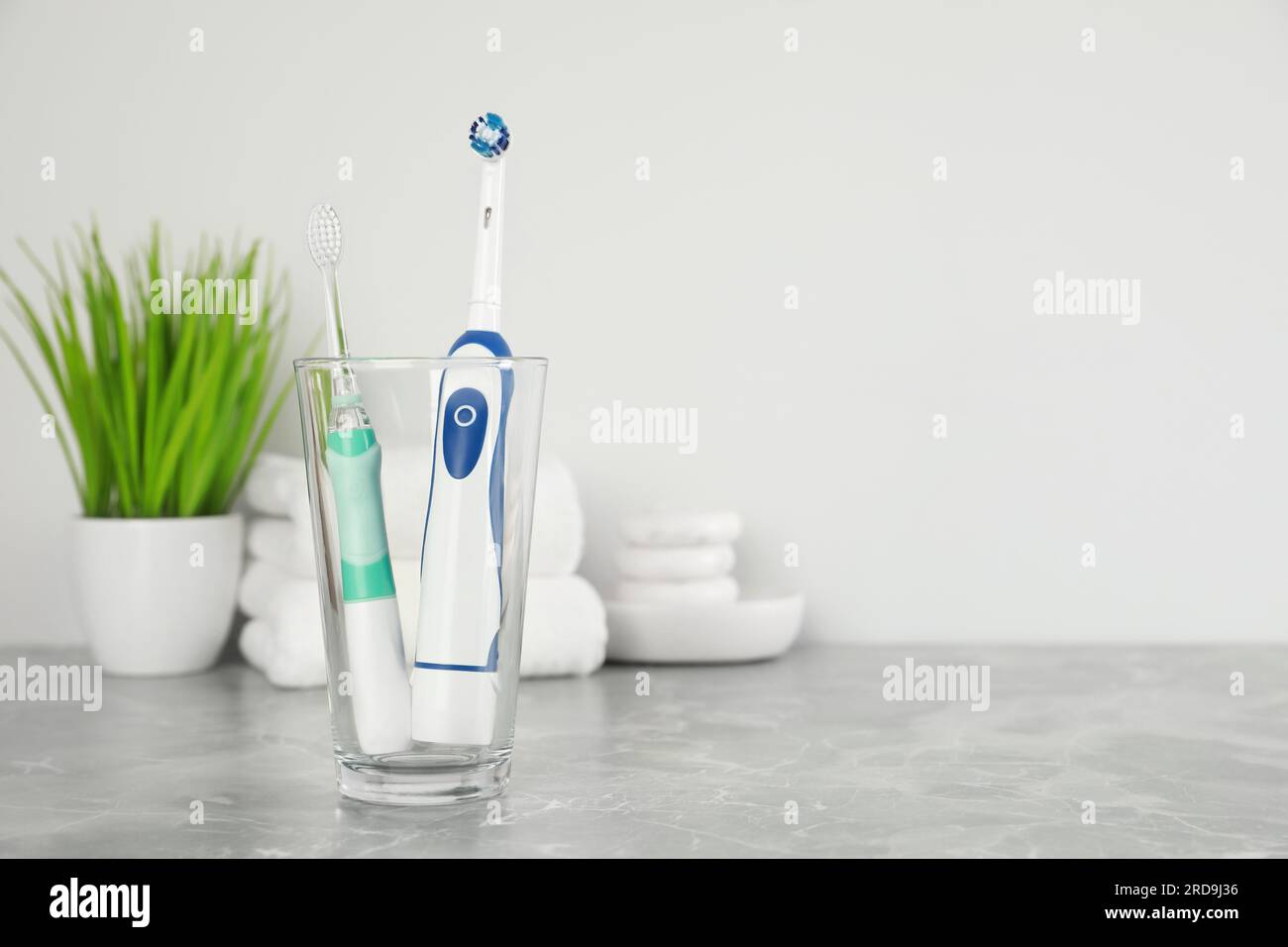 Electric toothbrushes in glass on light grey marble table, space for ...