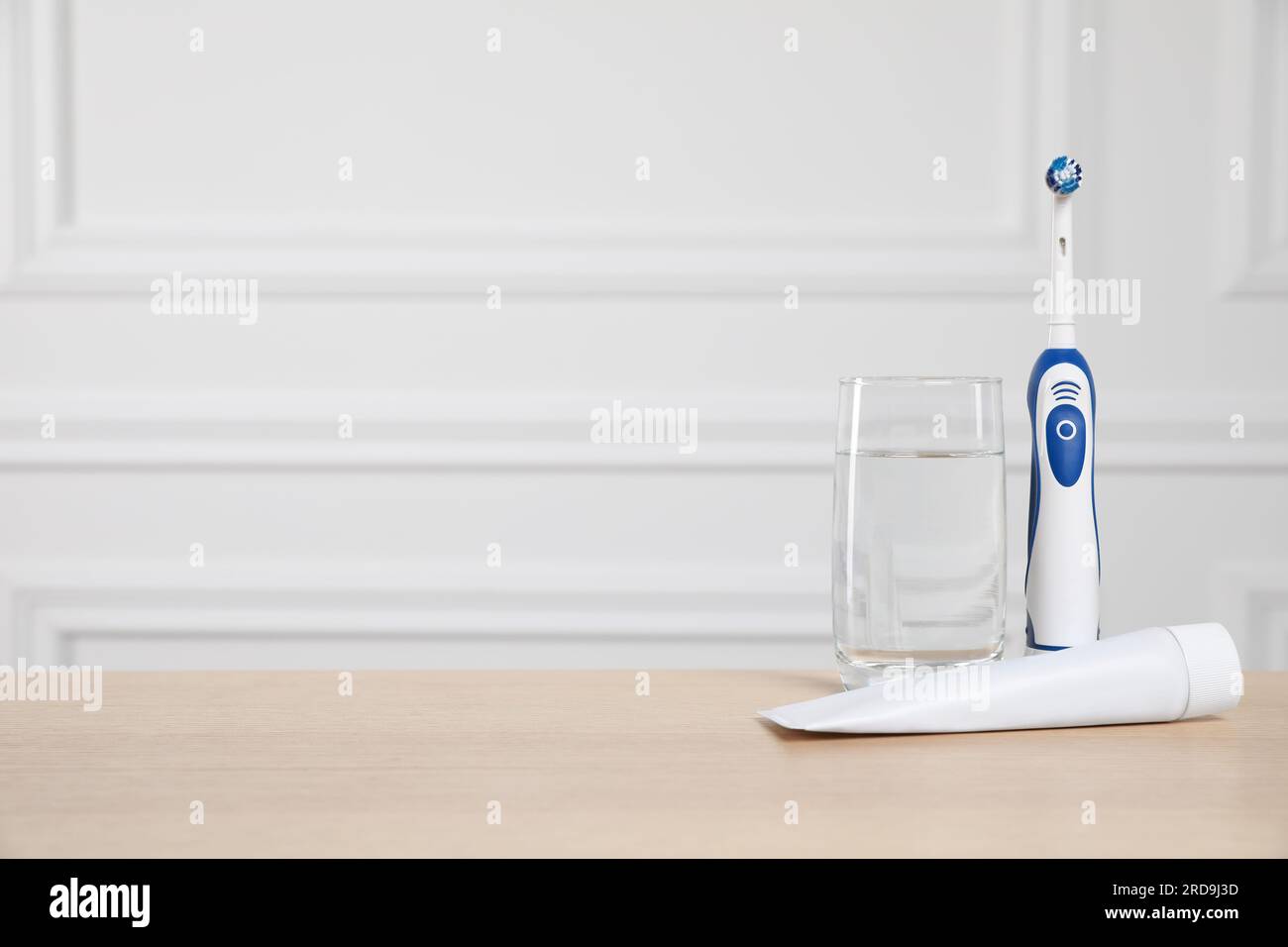 Electric toothbrush, glass of water and toothpaste on wooden table ...