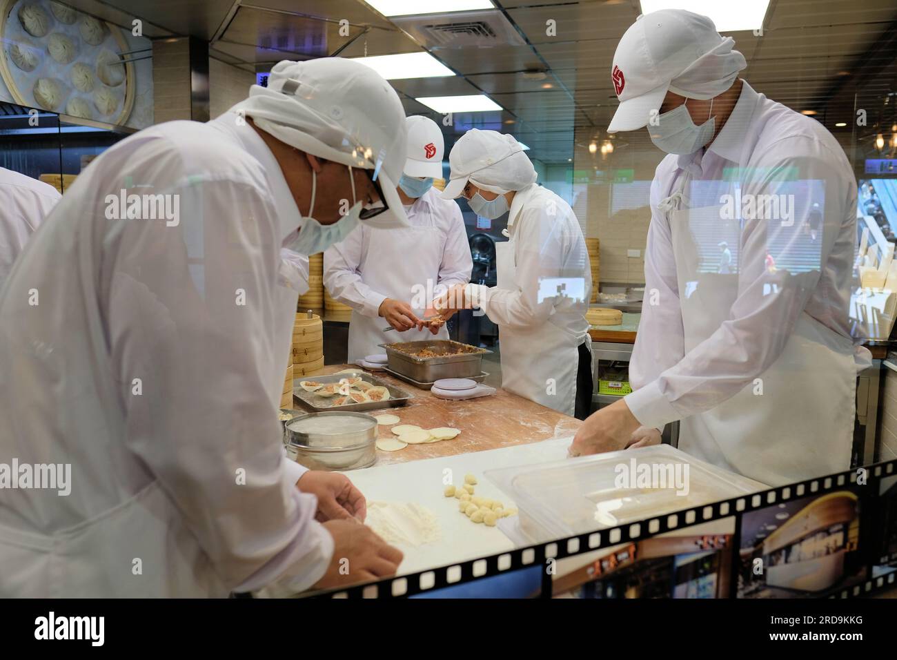Cooks and kitchen staff making dumplings, bao, and other Chinese dim ...