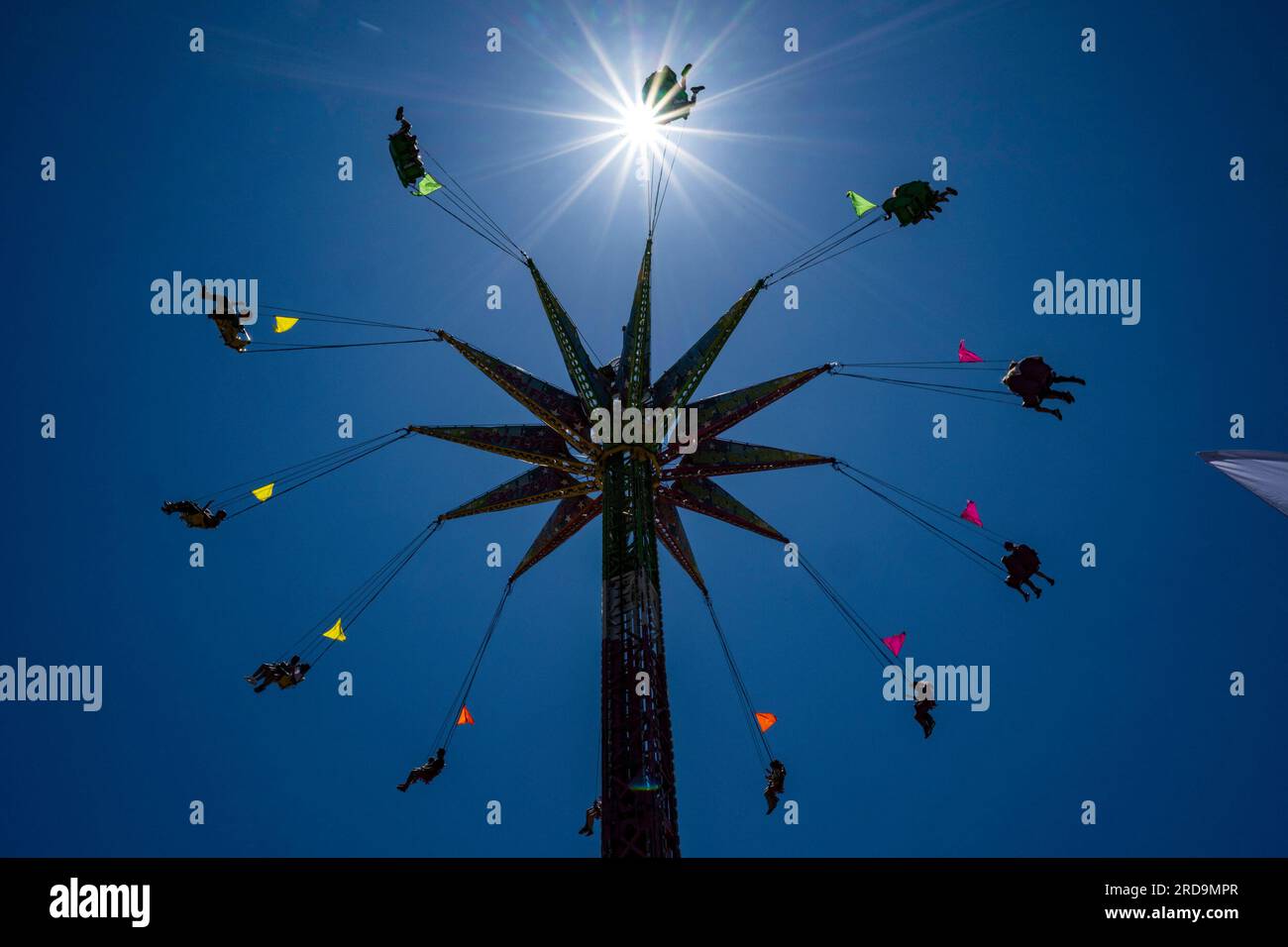 Under a sweltering summer sun, fairgoers fly through the air as they ...
