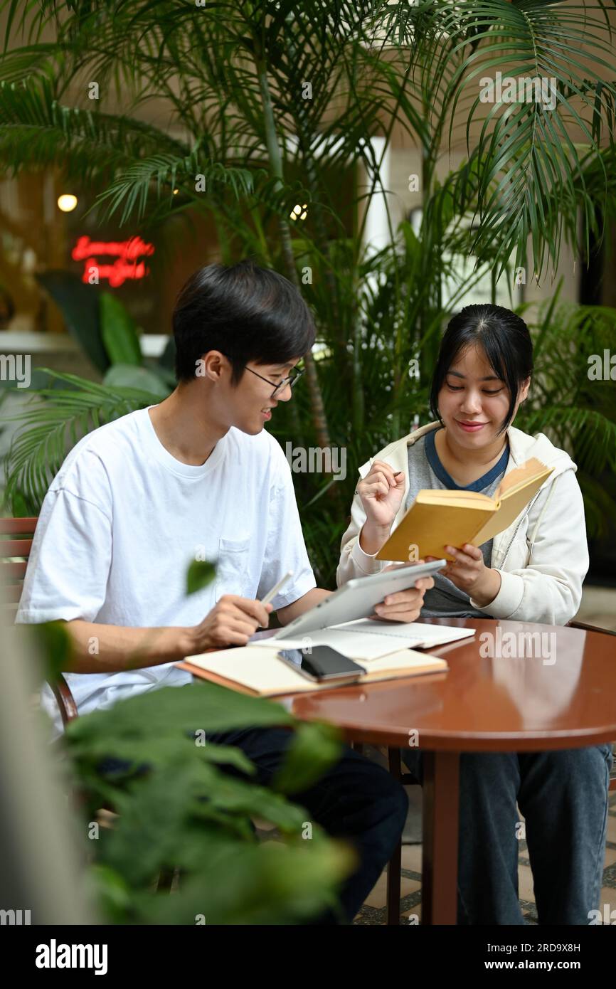 Two happy young Asian college students are sitting at a cafe in an ...
