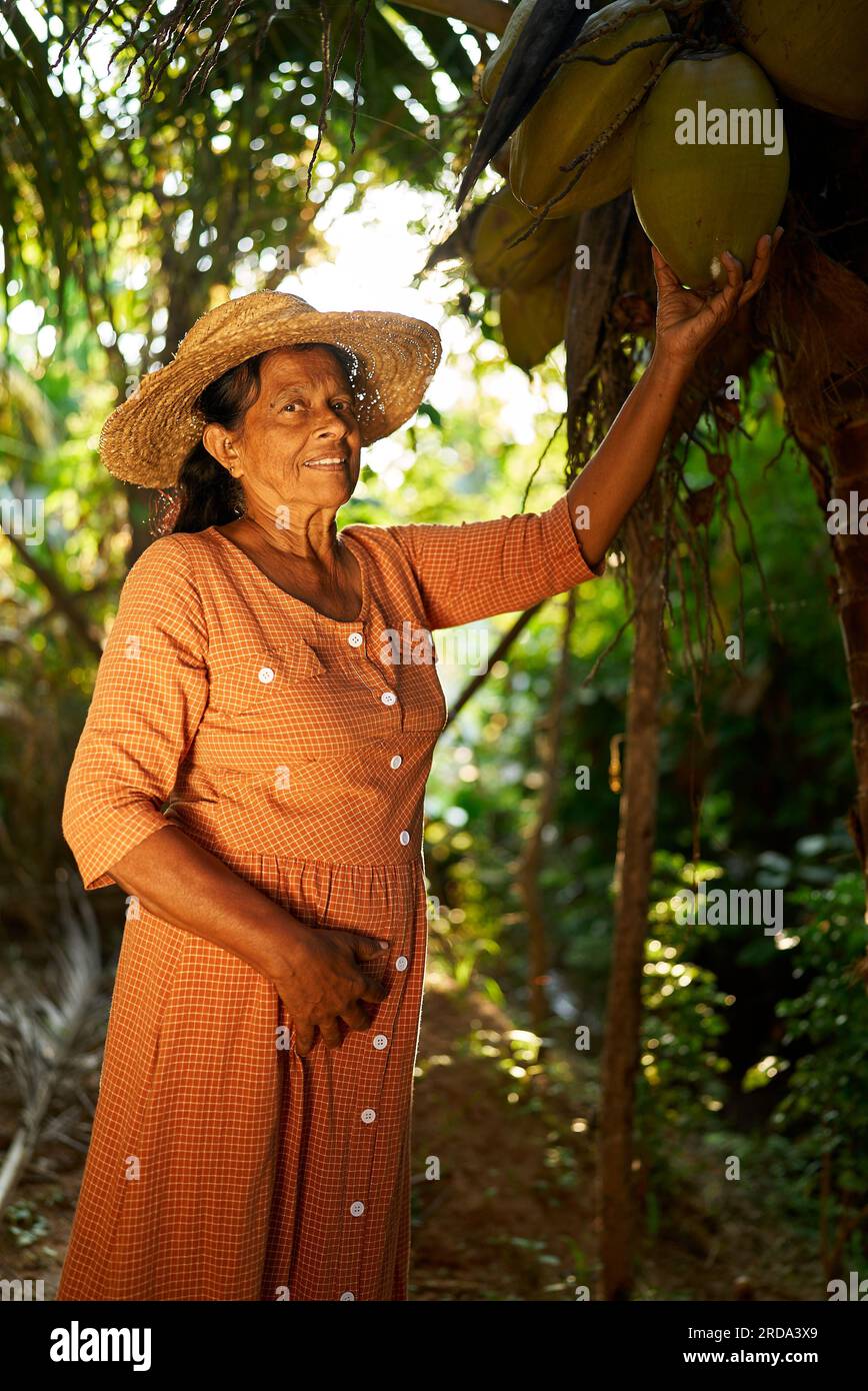 Elderly cheerful Indian female farmer in straw hat smiles holding ...