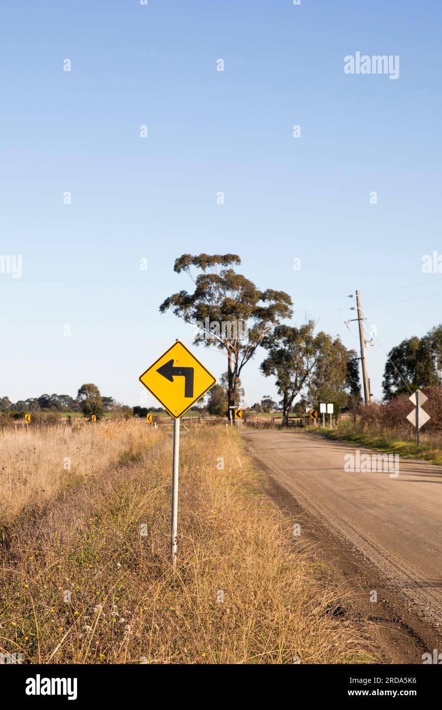 A rural dirt road stretches ahead, accompanied arrow warning sign ...