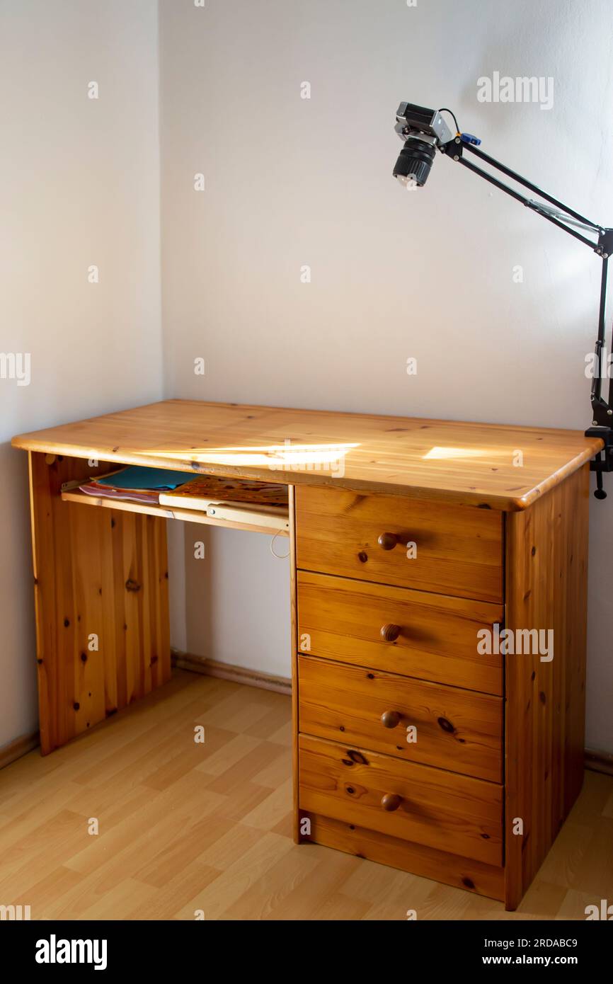 empty wooden writing desk, in a corner with white walls and sun rays ...