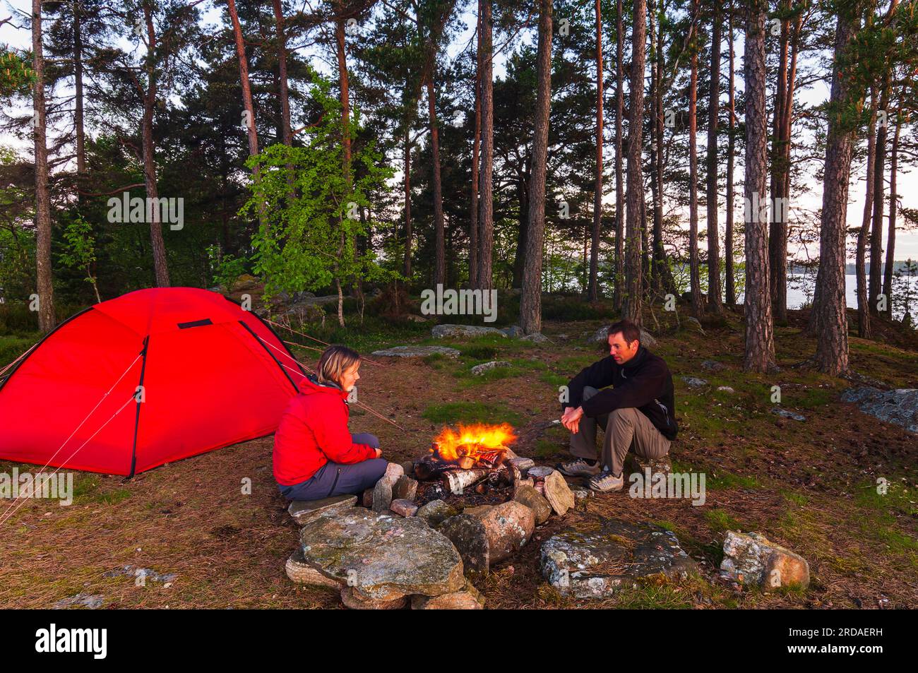 A young couple camping in the Swedish wilderness, sitting around a ...