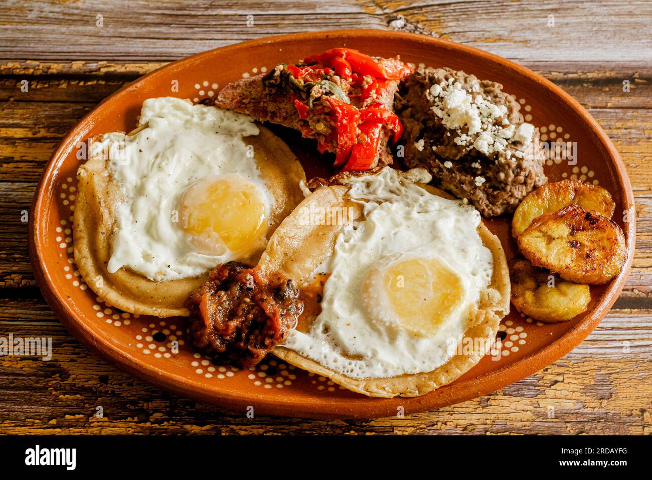 Huevos rancheros, meat, beans, and fried plantains in a clay dish ...