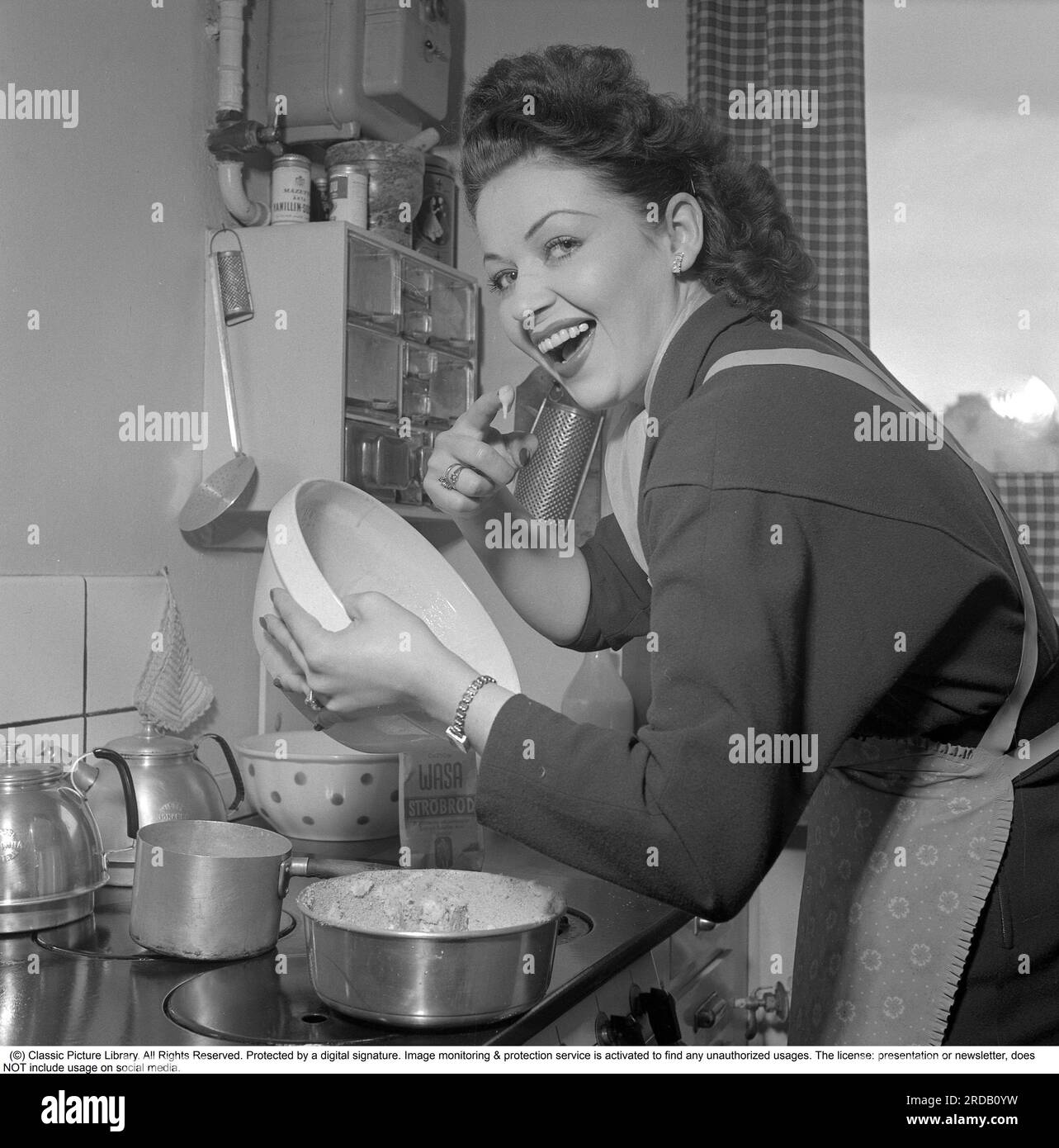 In the kitchen in the 1950s. A young woman in the kitchen making a cake ...