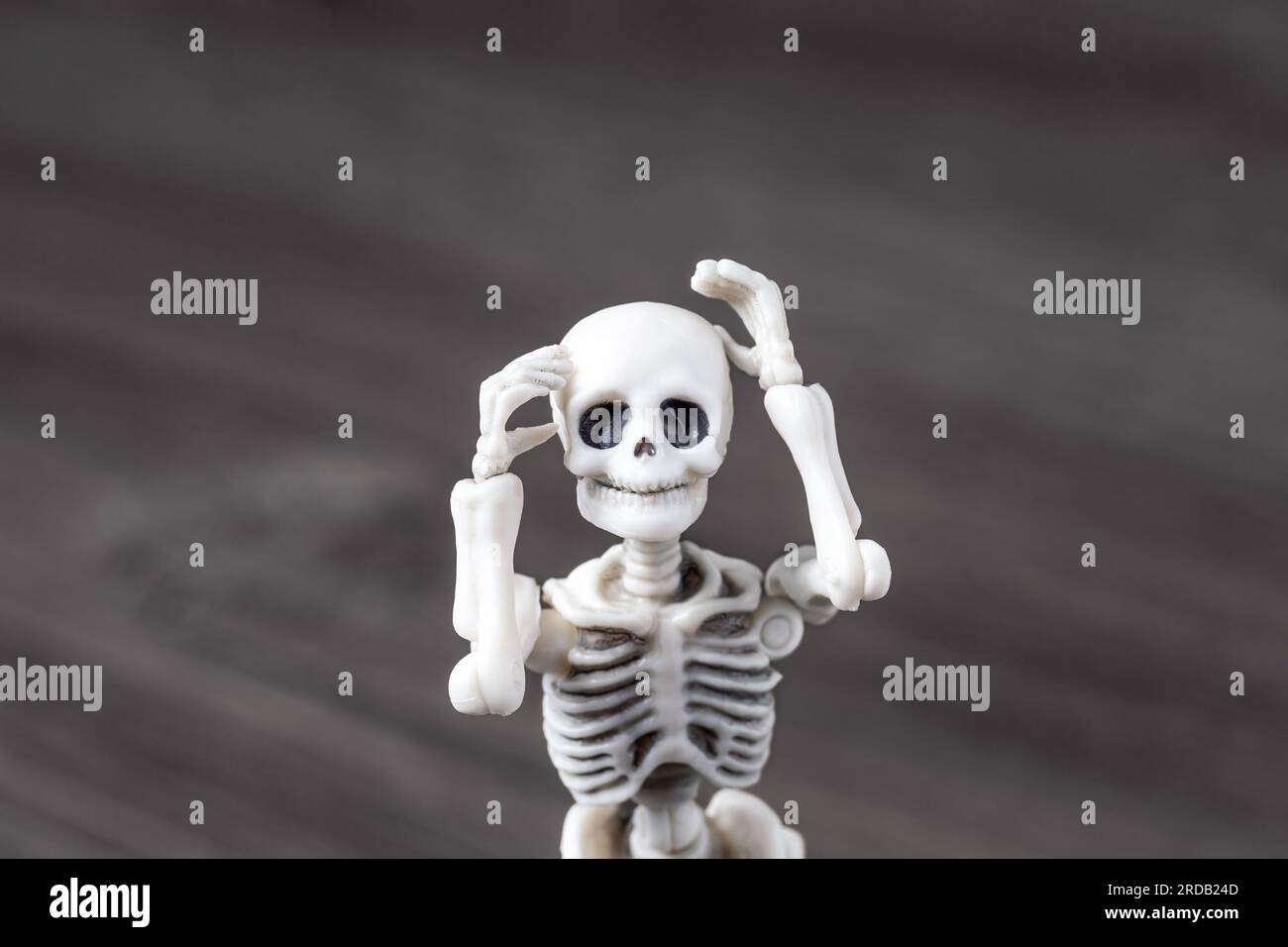 Skeleton figurine holding his head. Shocked funny figure on dark blurry ...
