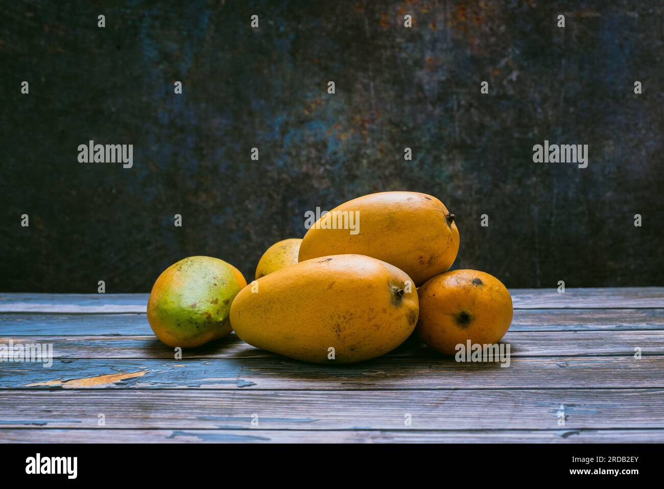 Group of ripe mangoes in dark environment on wooden table. Lateral view ...