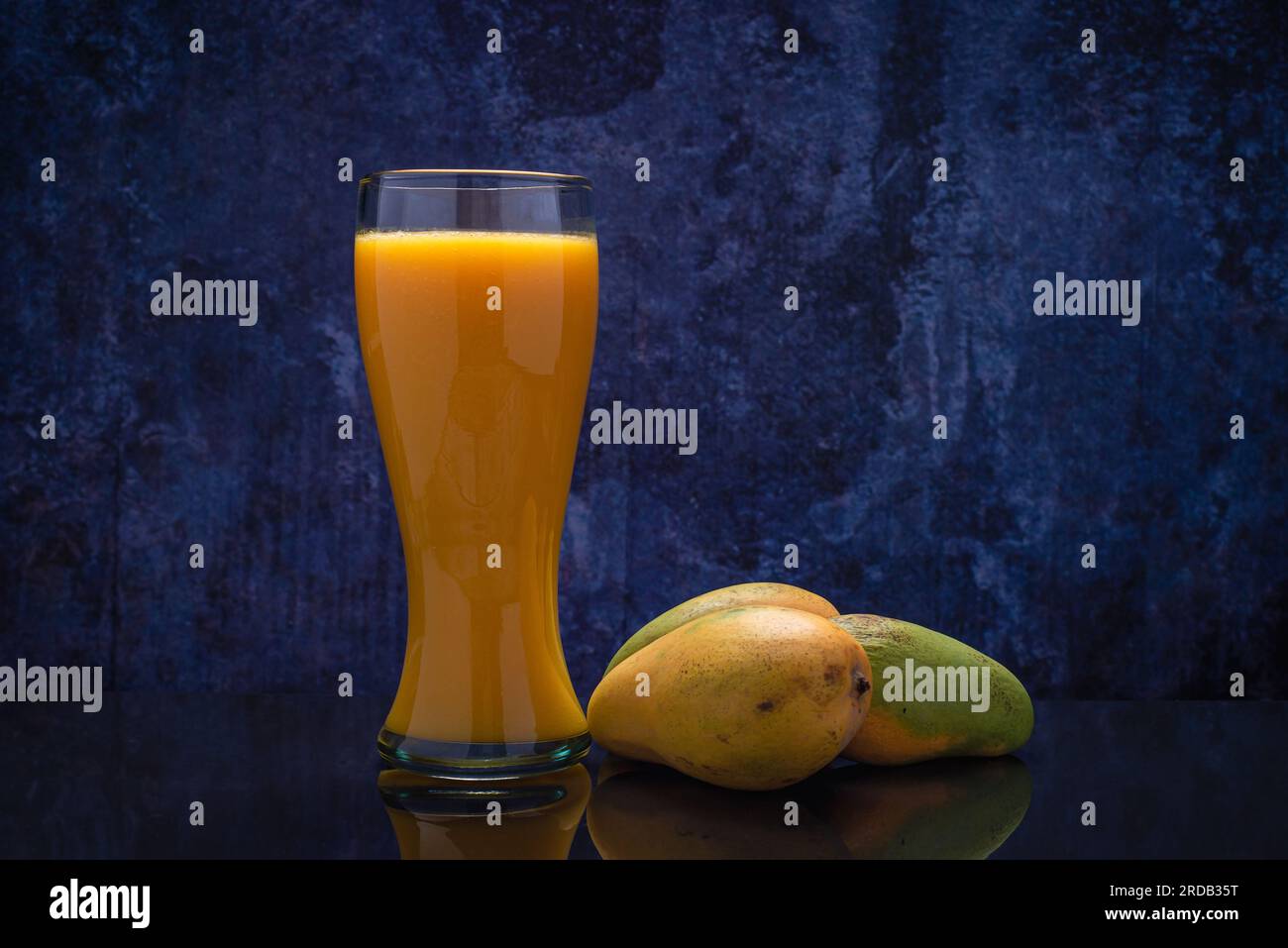 Mango juice glass and group of mangoes on black glass table. Blue ...