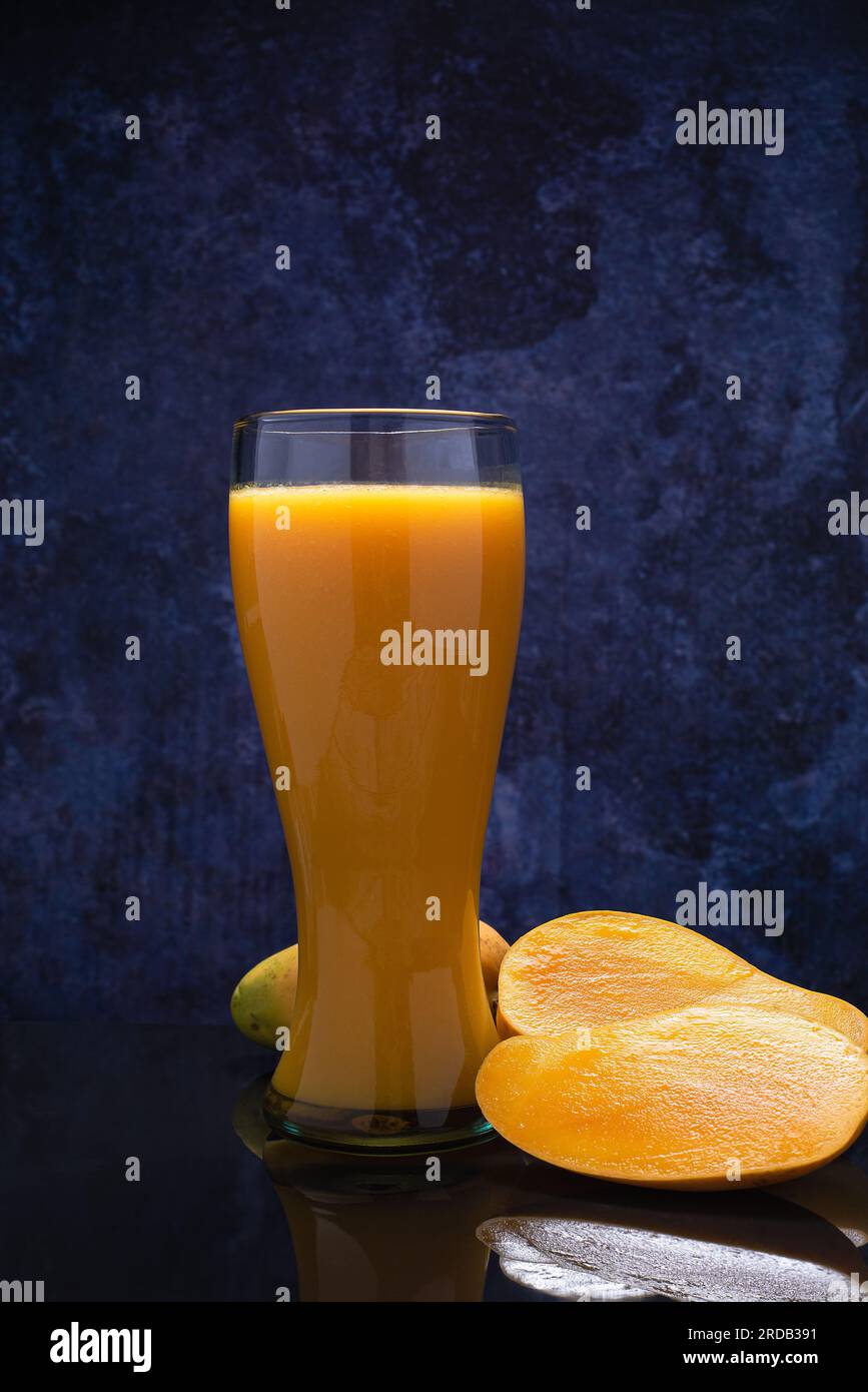 Mango juice glass and group of mangoes on black glass table. Blue ...