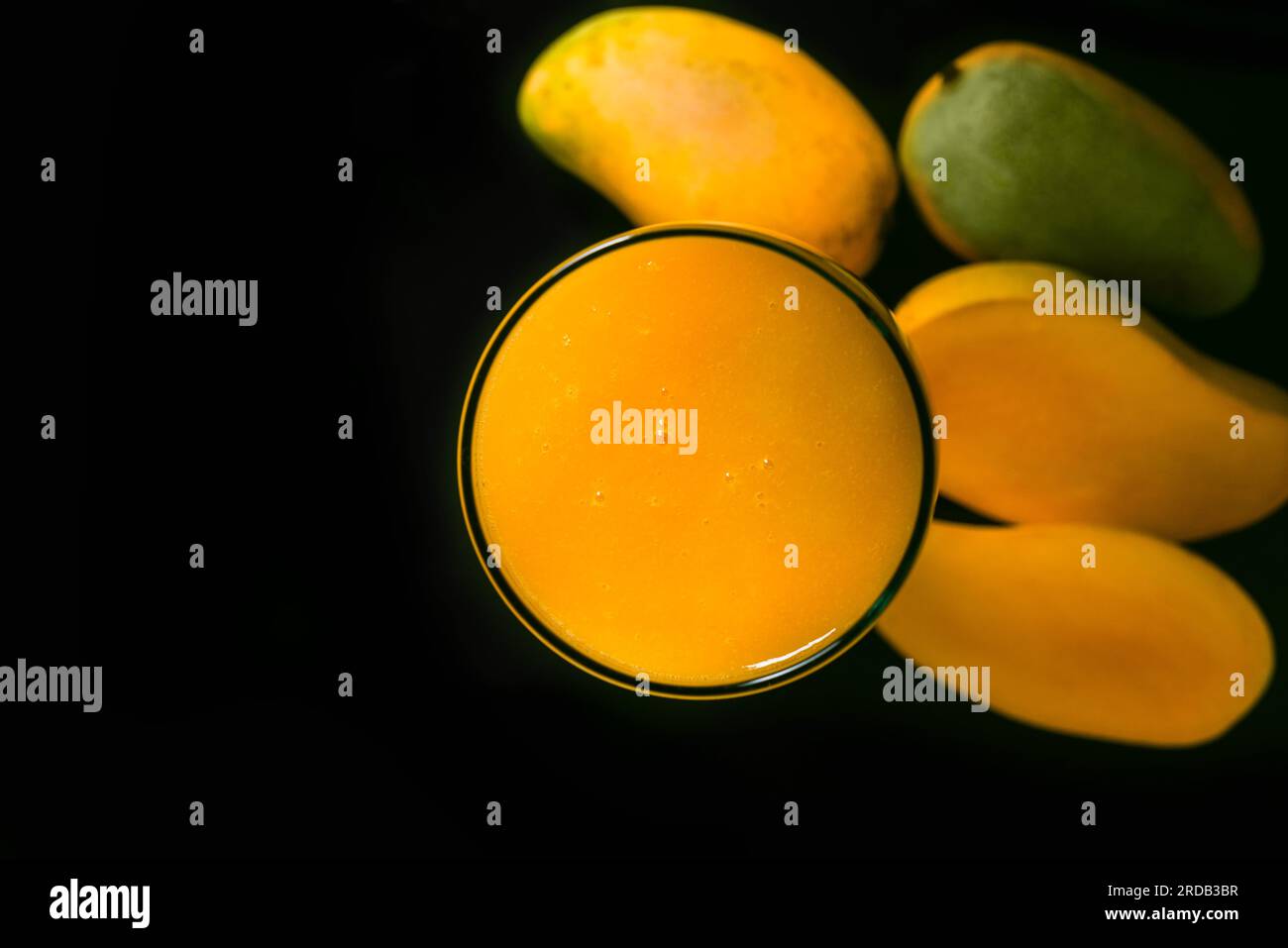 Mango juice glass and group of mangoes on black glass table. Blue ...