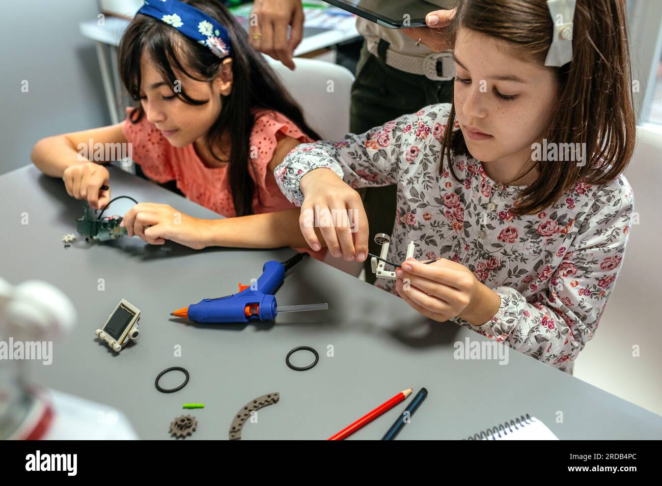 Students assembling machine pieces with teacher helping their in a ...