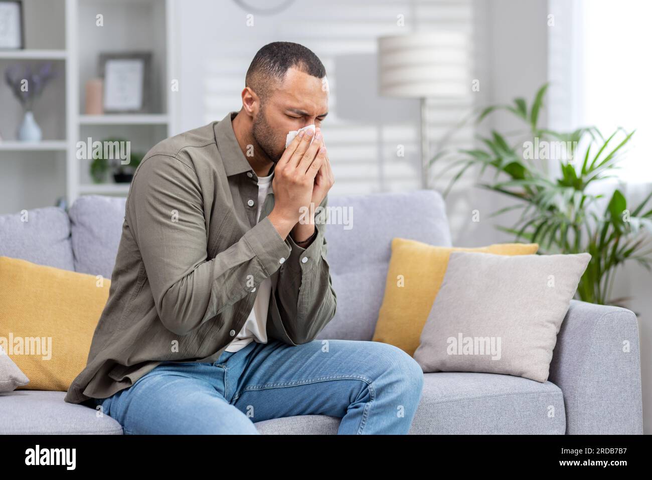 African American man sick at home. He sits on the couch and blows his ...