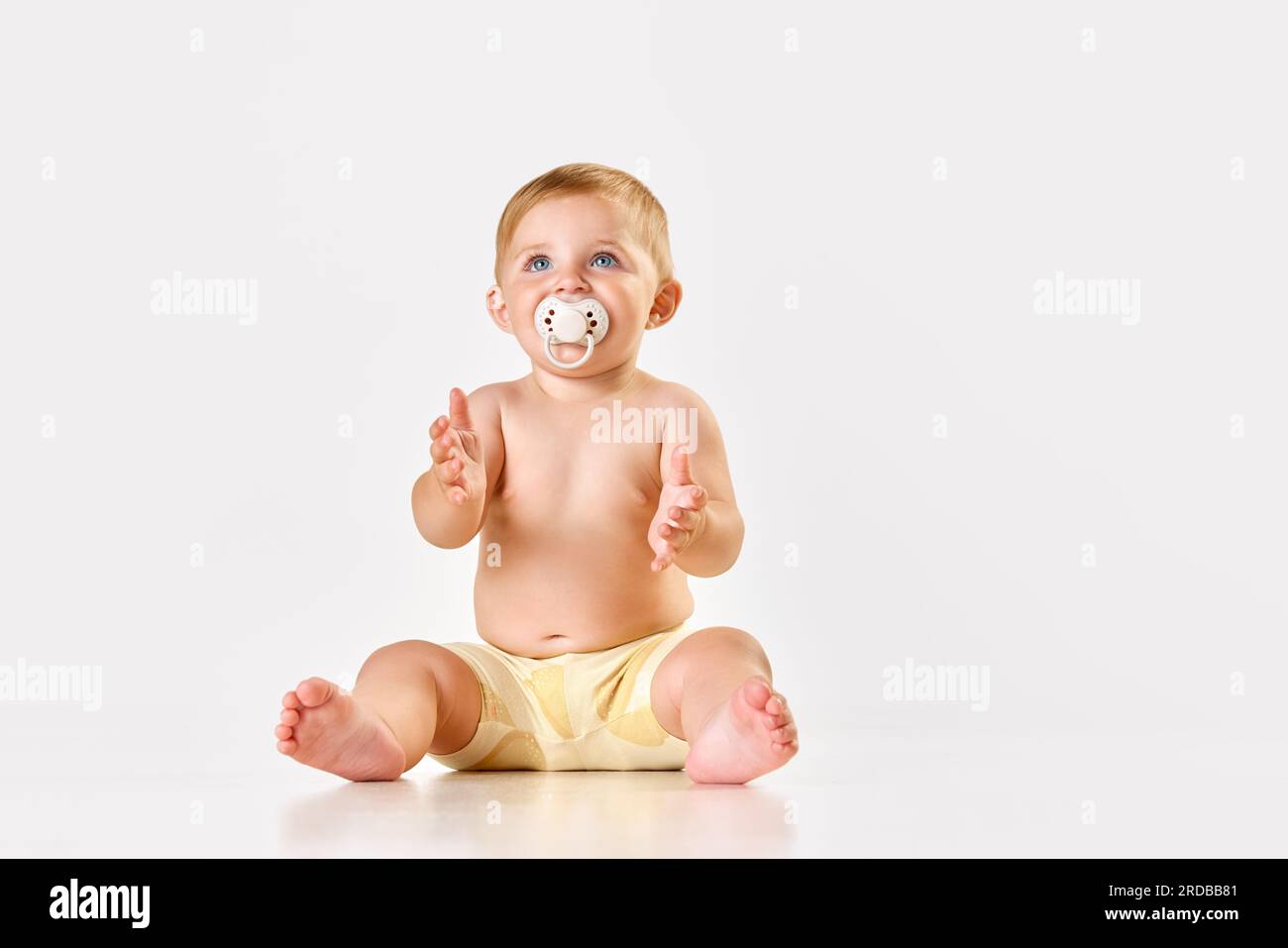 Portrait of little calm baby, toddler sitting with pacifier, clapping ...