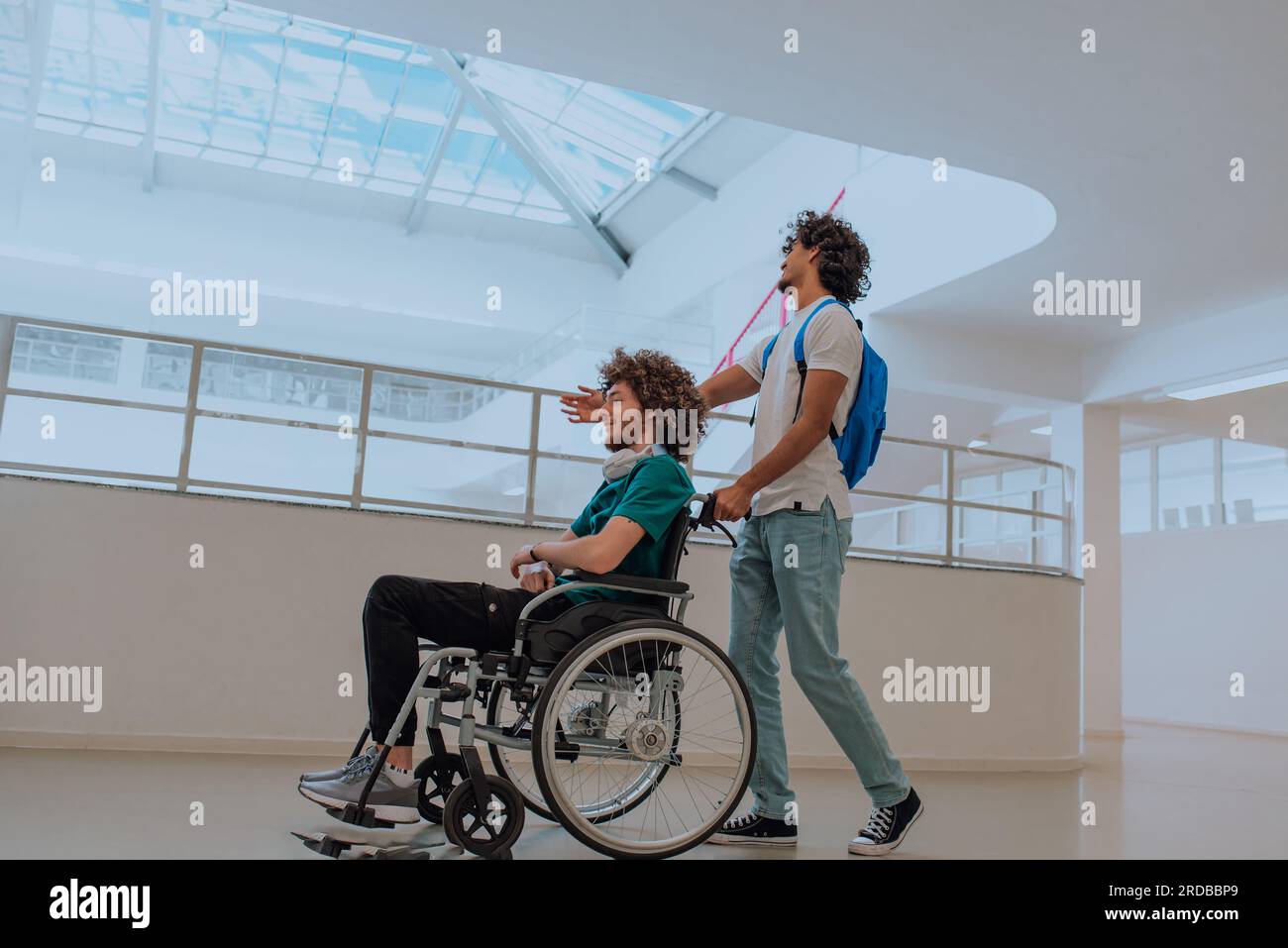 African American student pushing his friend's wheelchair through a modern school, demonstrating ...