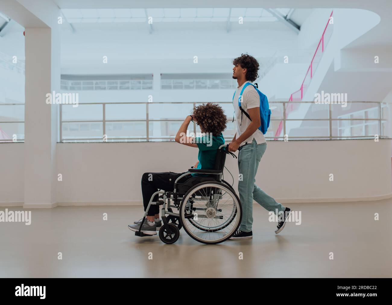 African American student pushing his friend's wheelchair through a ...