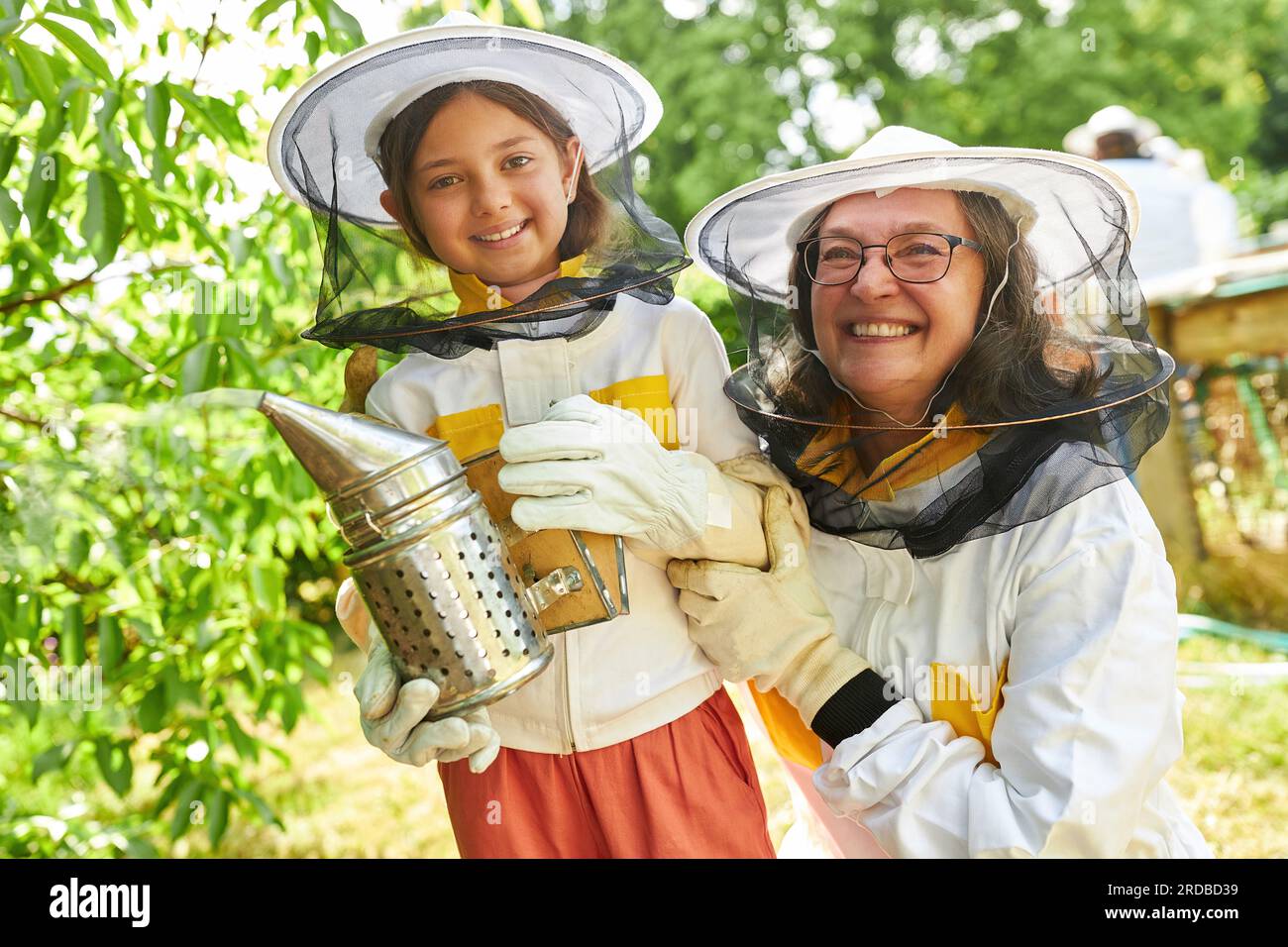 Portrait of happy senior female beekeeper with girl holding smoker in ...