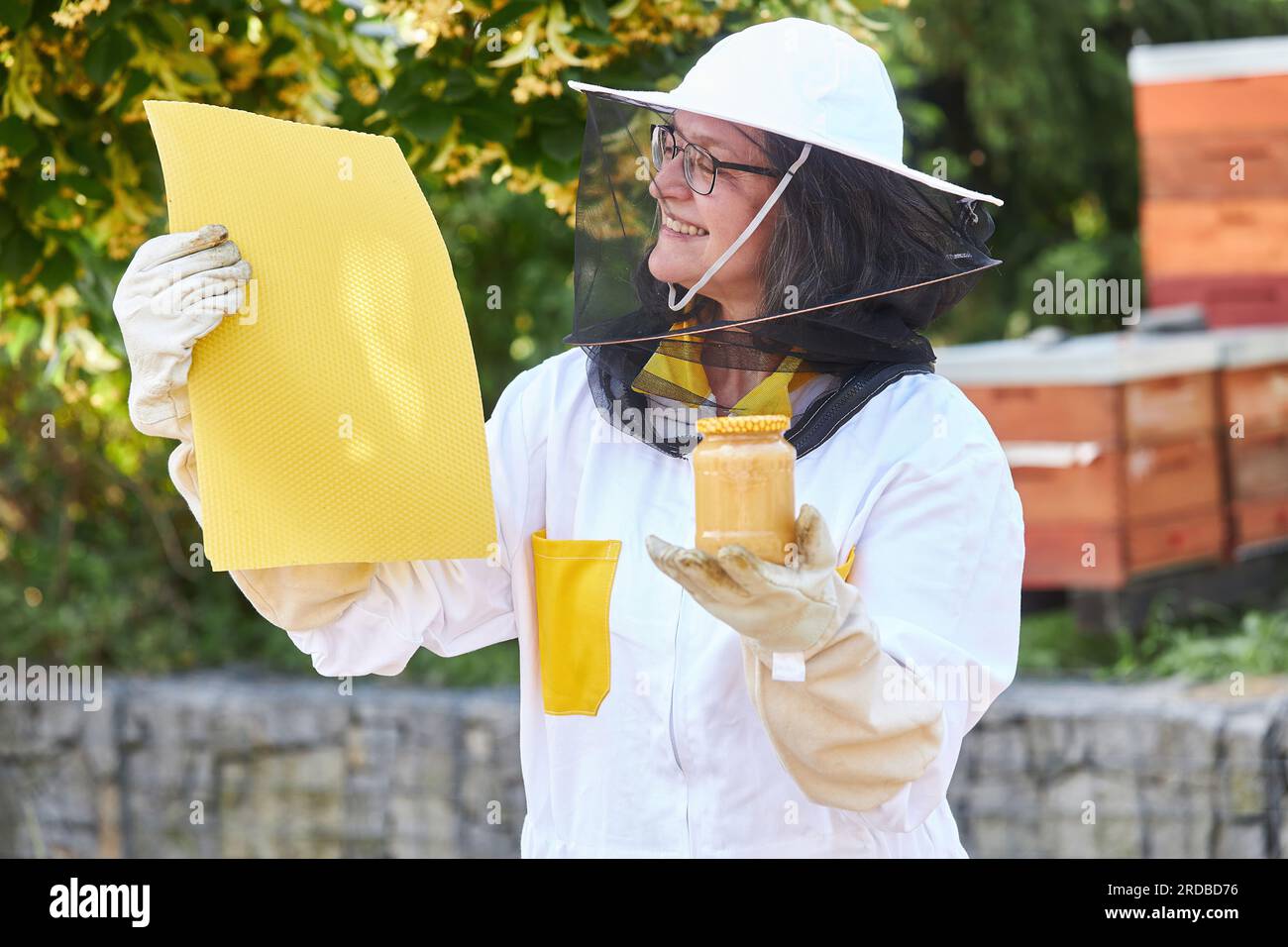Female beekeeper offering honey jar and beeswax sheets in front of ...