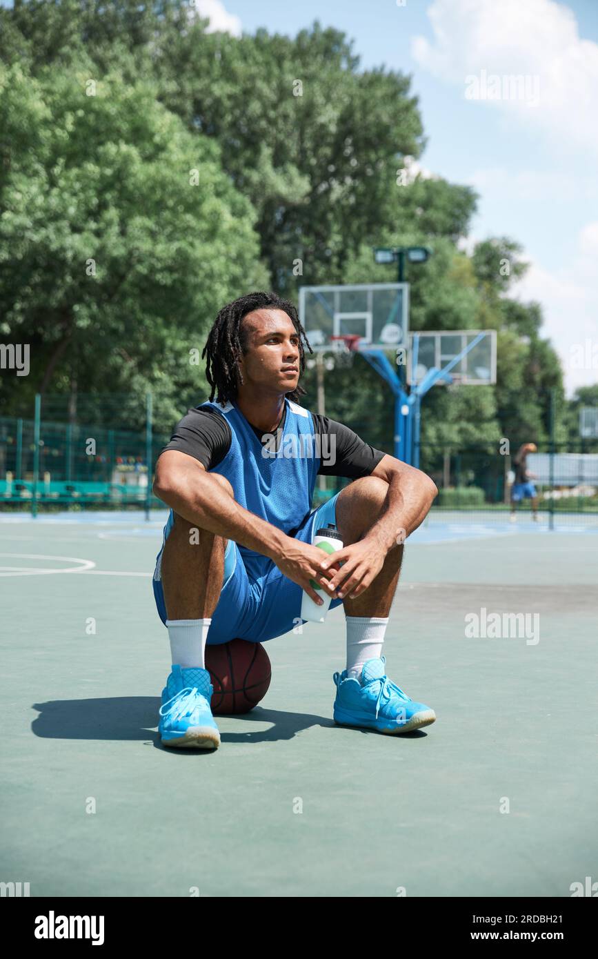 Young man with dreads, athlete in blue uniform sitting on basketball ...