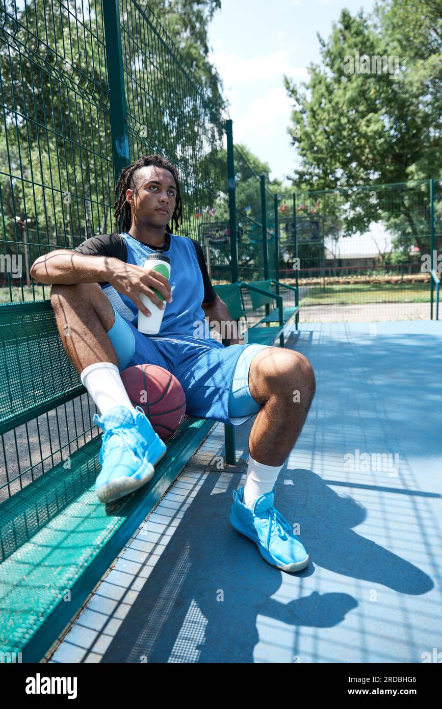 Young man with dreads in blue uniform sitting on bench after playing ...