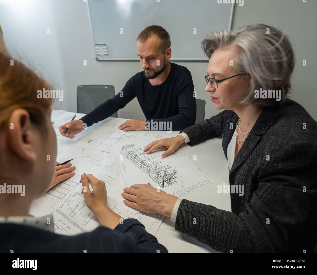 Four business people sitting around a table discussing blueprints ...