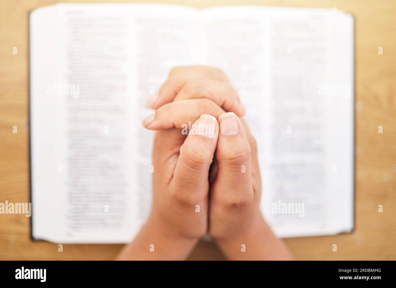 Hands, bible and desk for prayer, closeup and mindfulness for faith, religion or reading in pov ...