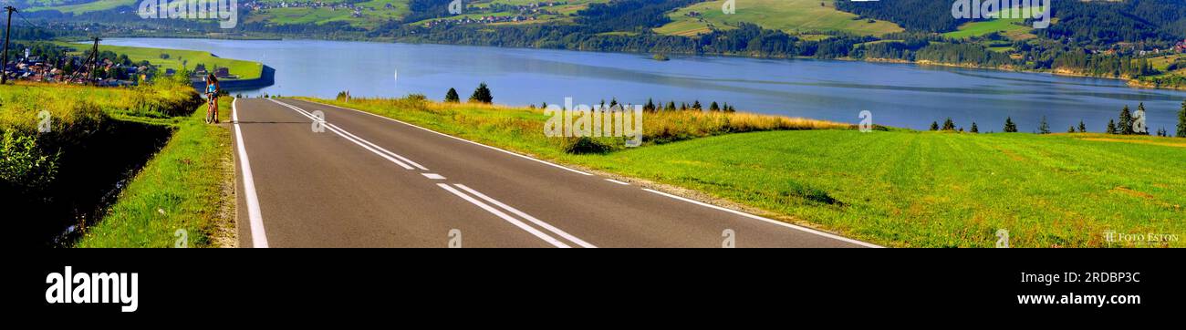 An asphalt two-way road in the mountains, with a lake and forests in ...