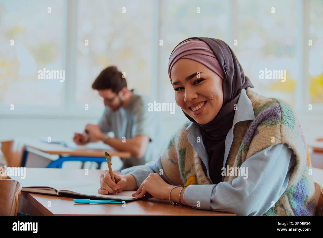 A Muslim hijab student sitting in a modern classroom, attentively ...
