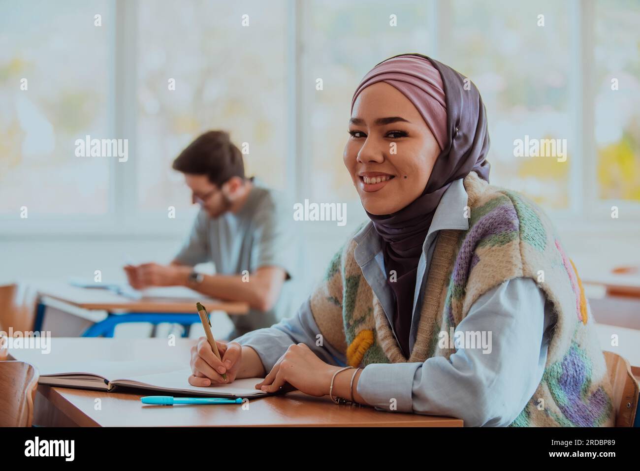 A Muslim hijab student sitting in a modern classroom, attentively ...