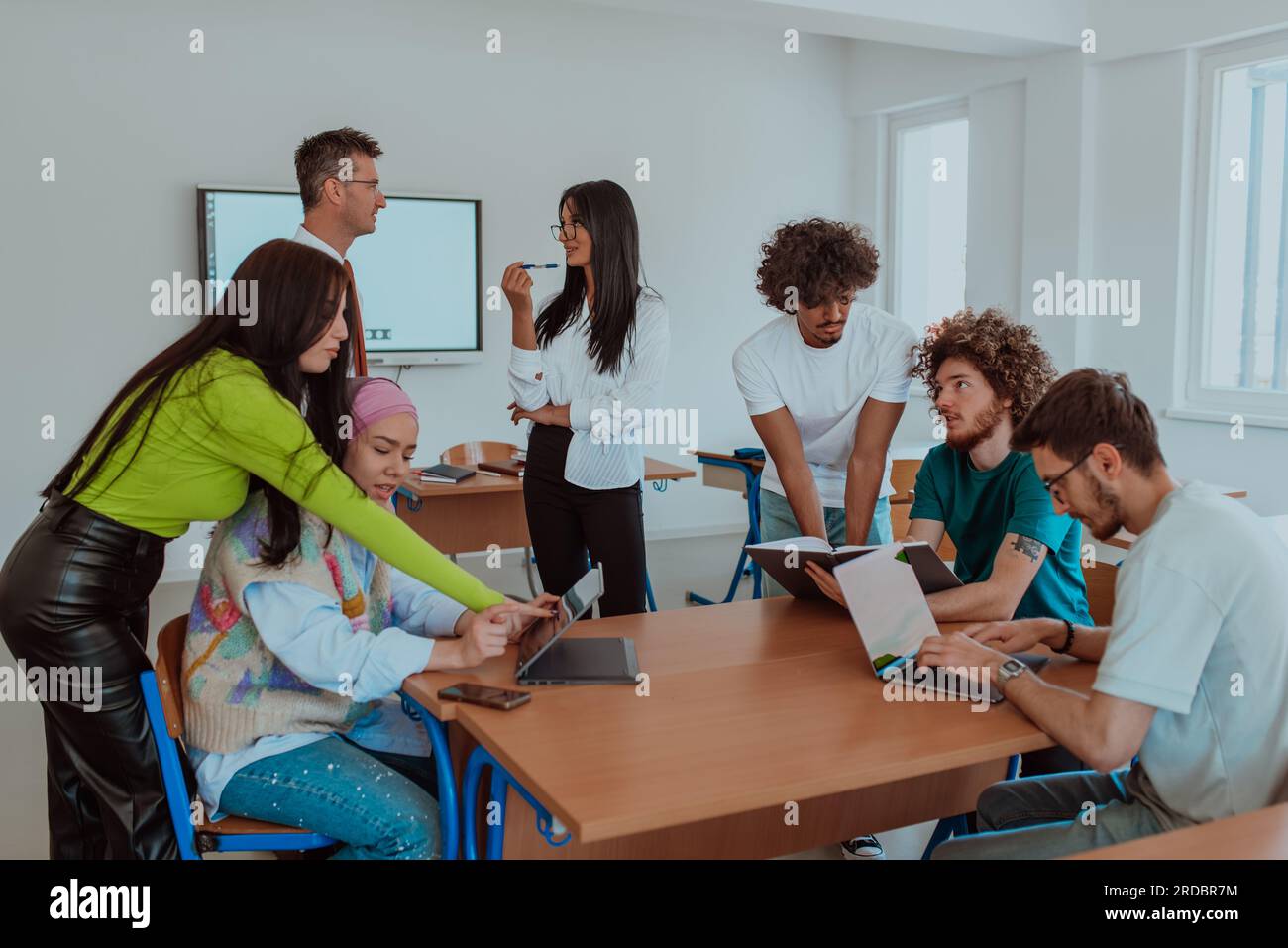 A diverse group of students gathers in a modern school classroom ...