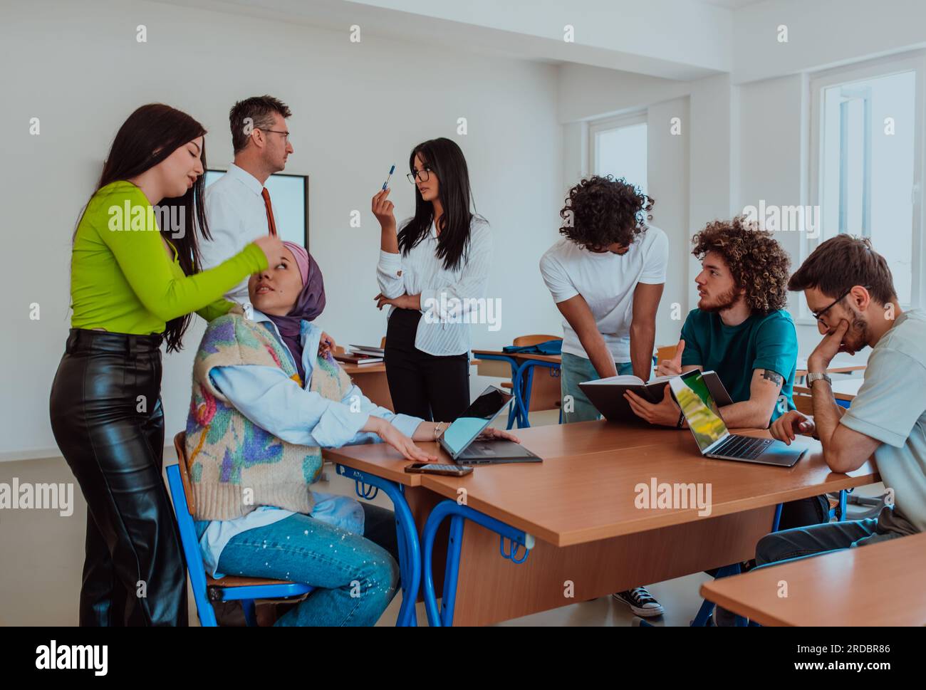 A diverse group of students gathers in a modern school classroom ...