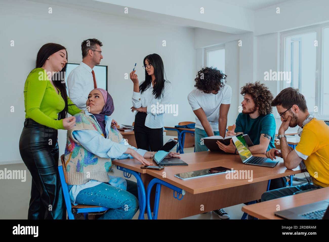 A diverse group of students gathers in a modern school classroom ...